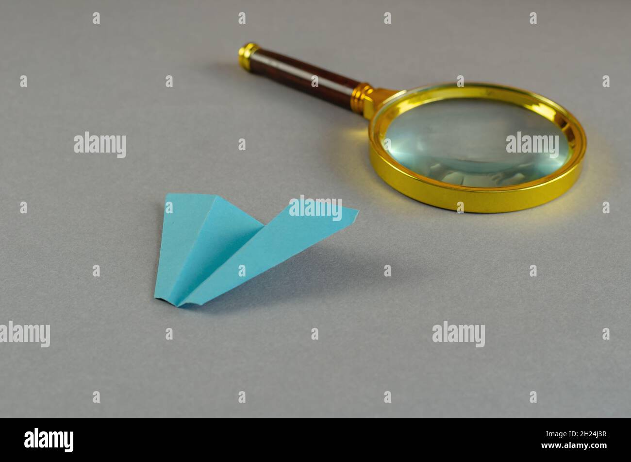 Blue paper airplane and magnifying glass on gray background. Small ...