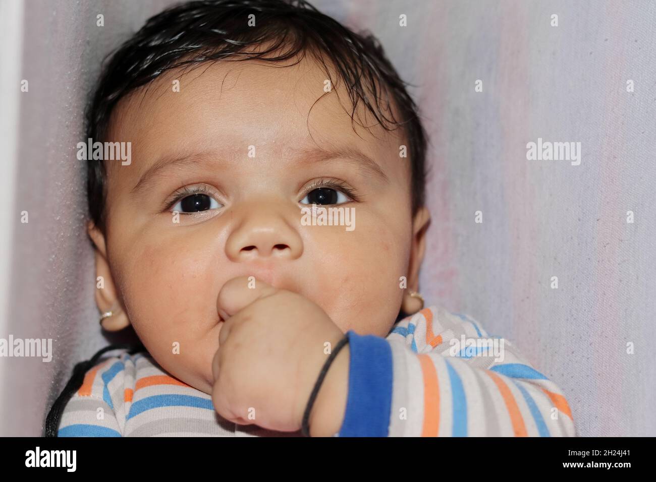 Close-up of An indian little newborn innocent baby sucking fingers with ...