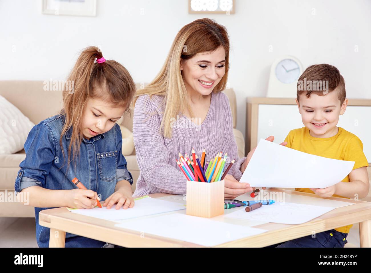 Cute little children and their nanny drawing at home Stock Photo - Alamy