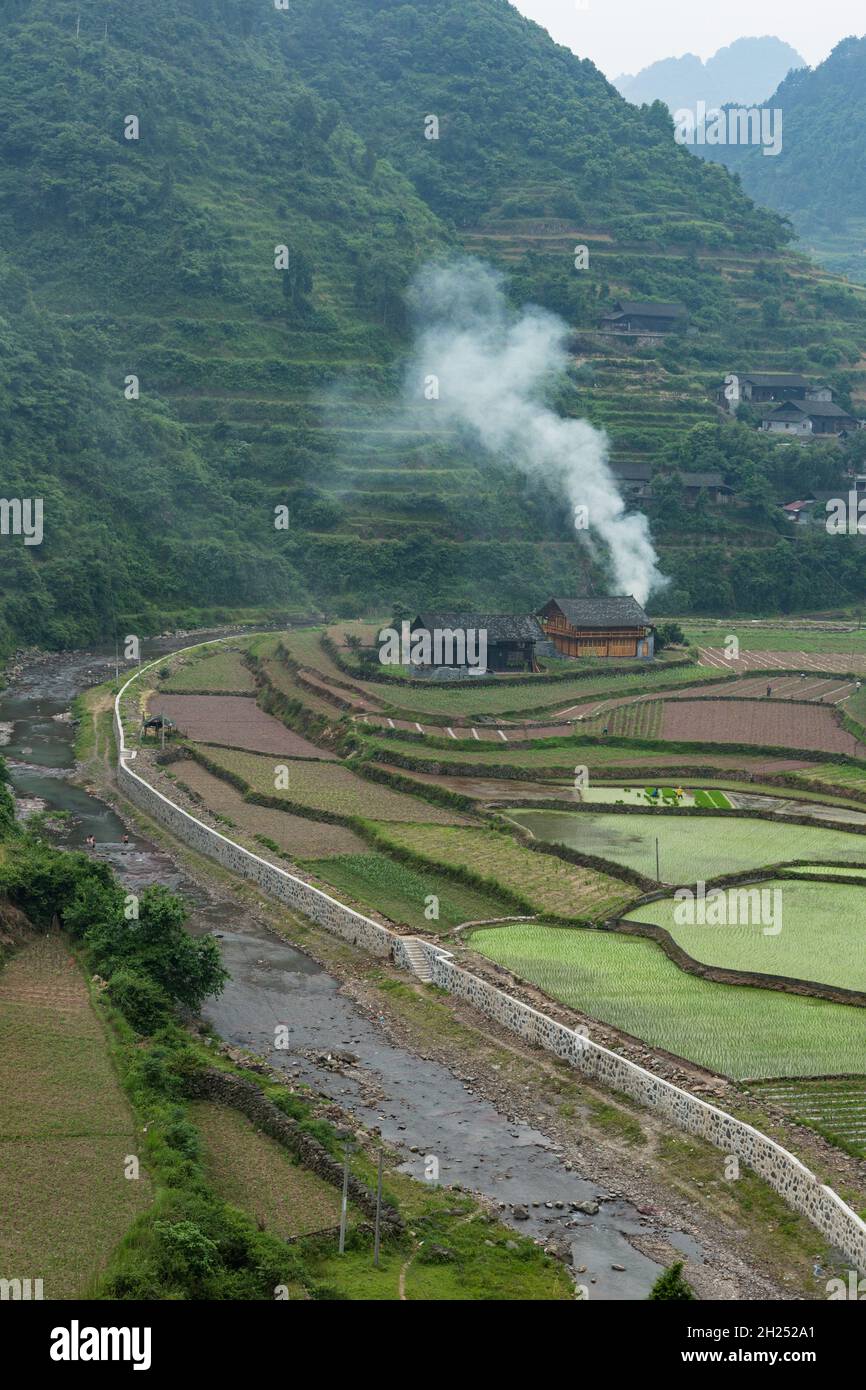 Smoke rises from a farm house surrounded by terraced rice paddies in ...