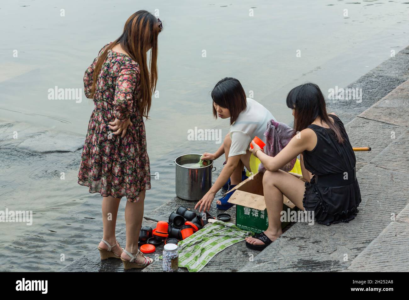 Women washing up dishes with river water on the bank of the Tuojiang ...