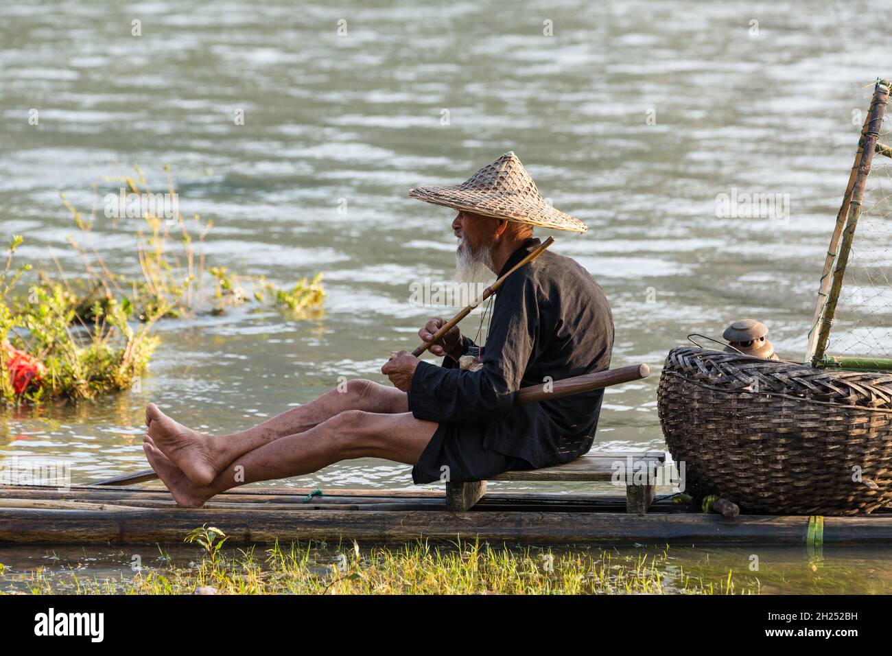 Elderly traditional cormorant fisherman smokes a wooden pipe on his ...