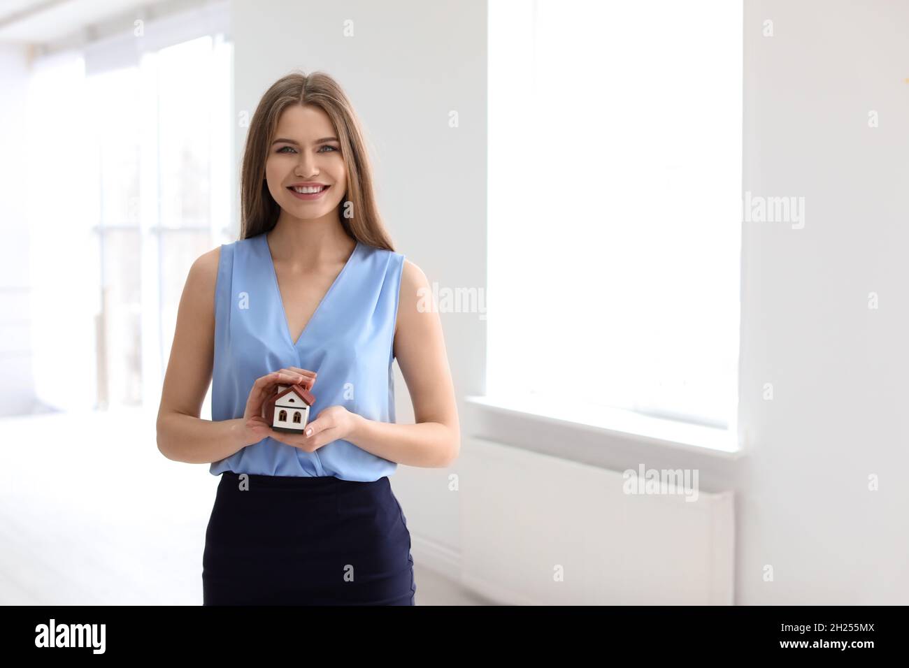 Beautiful real estate agent with house model indoors Stock Photo - Alamy