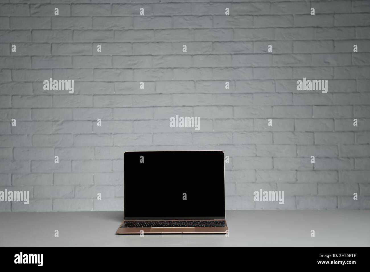 Modern laptop with blank screen on table against brick wall Stock Photo ...