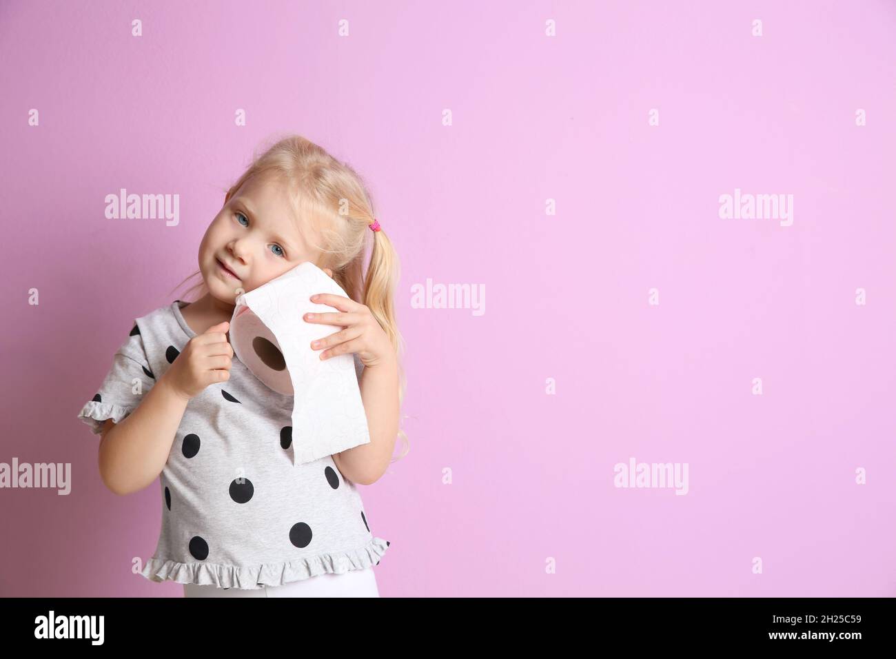 Cute little girl holding toilet paper roll on color background. Space ...