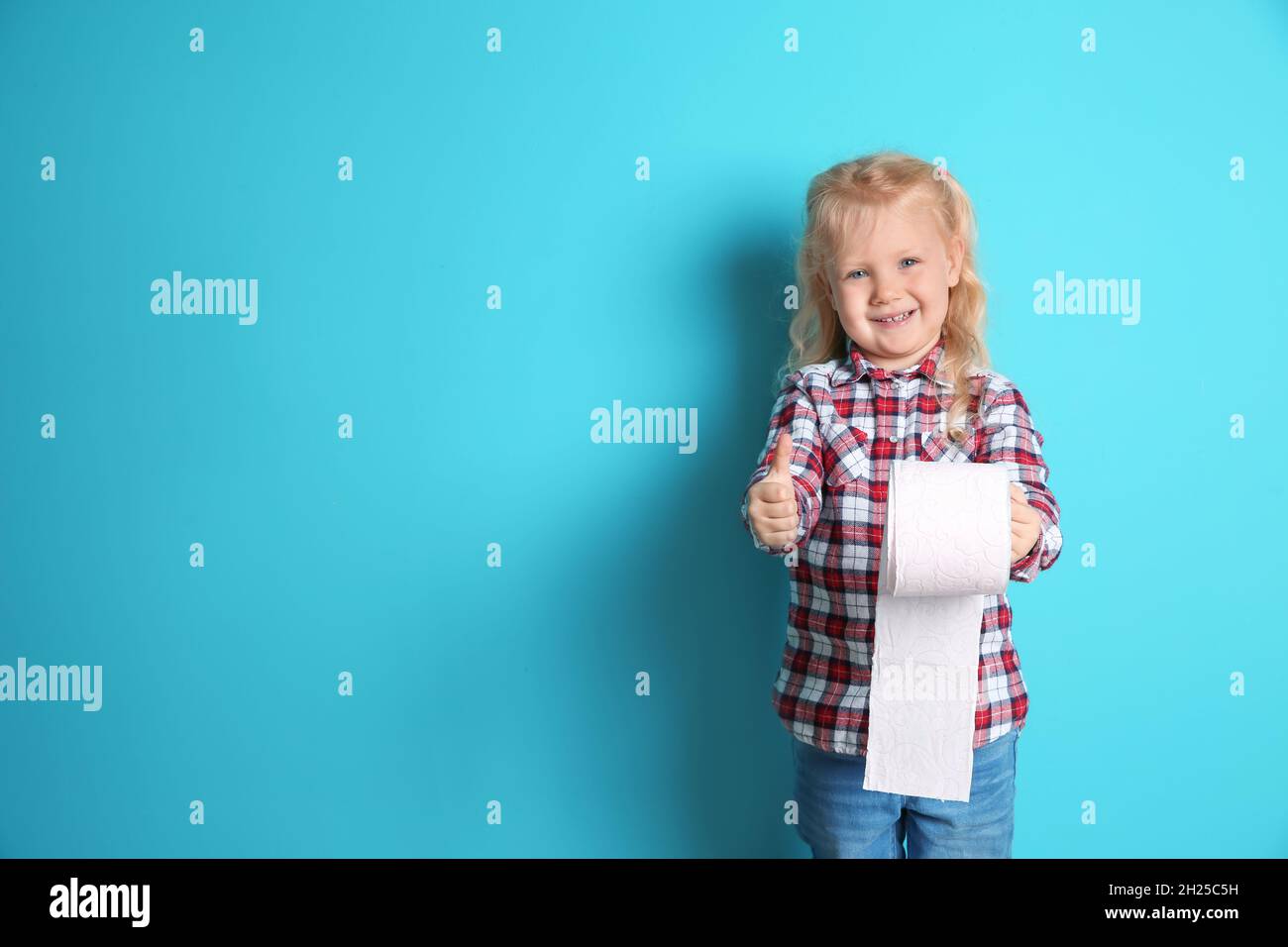 Cute little girl holding toilet paper roll on color background. Space ...