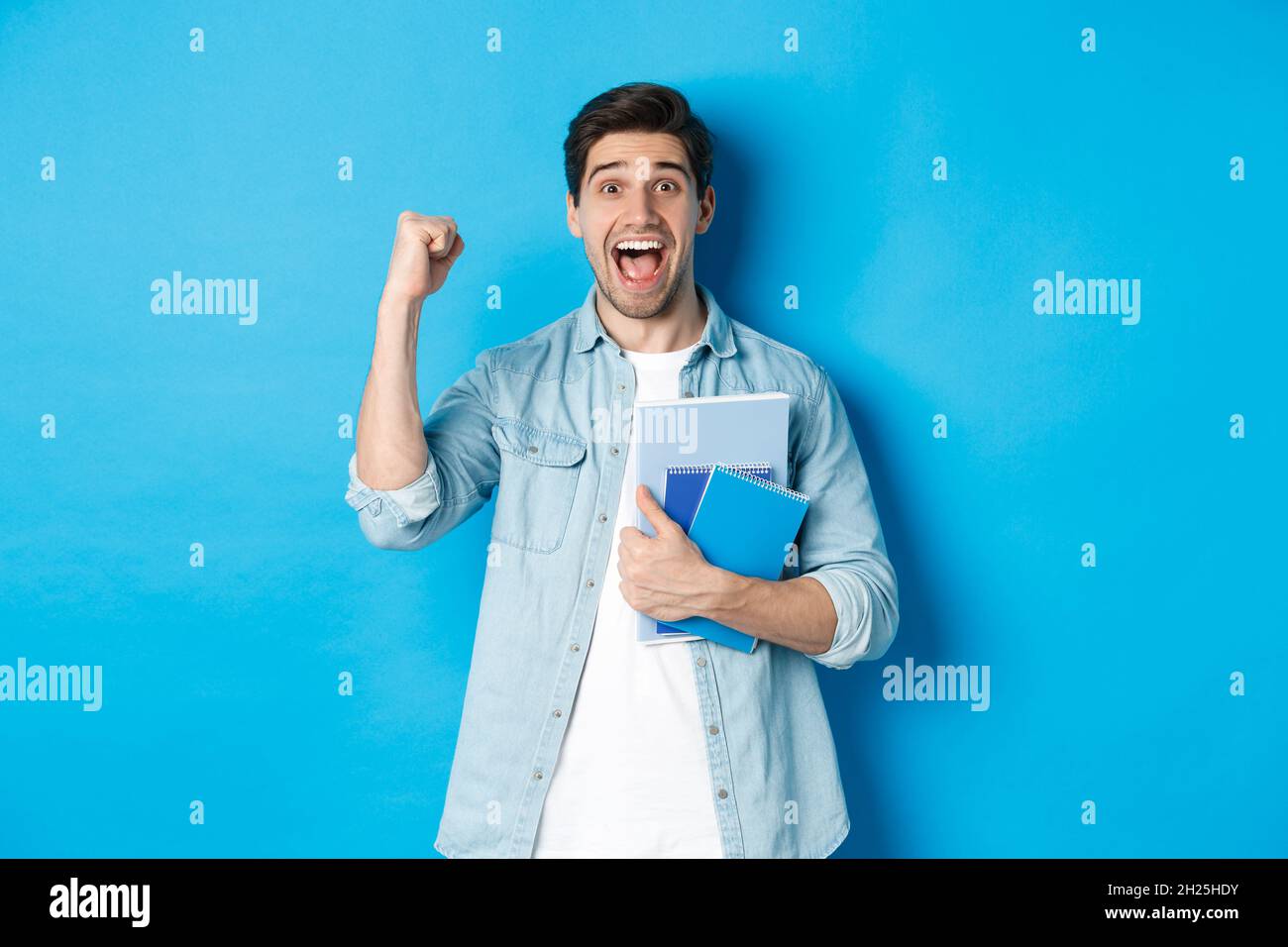 Cheerful guy holding notebooks and celebrating, making fist pump and ...