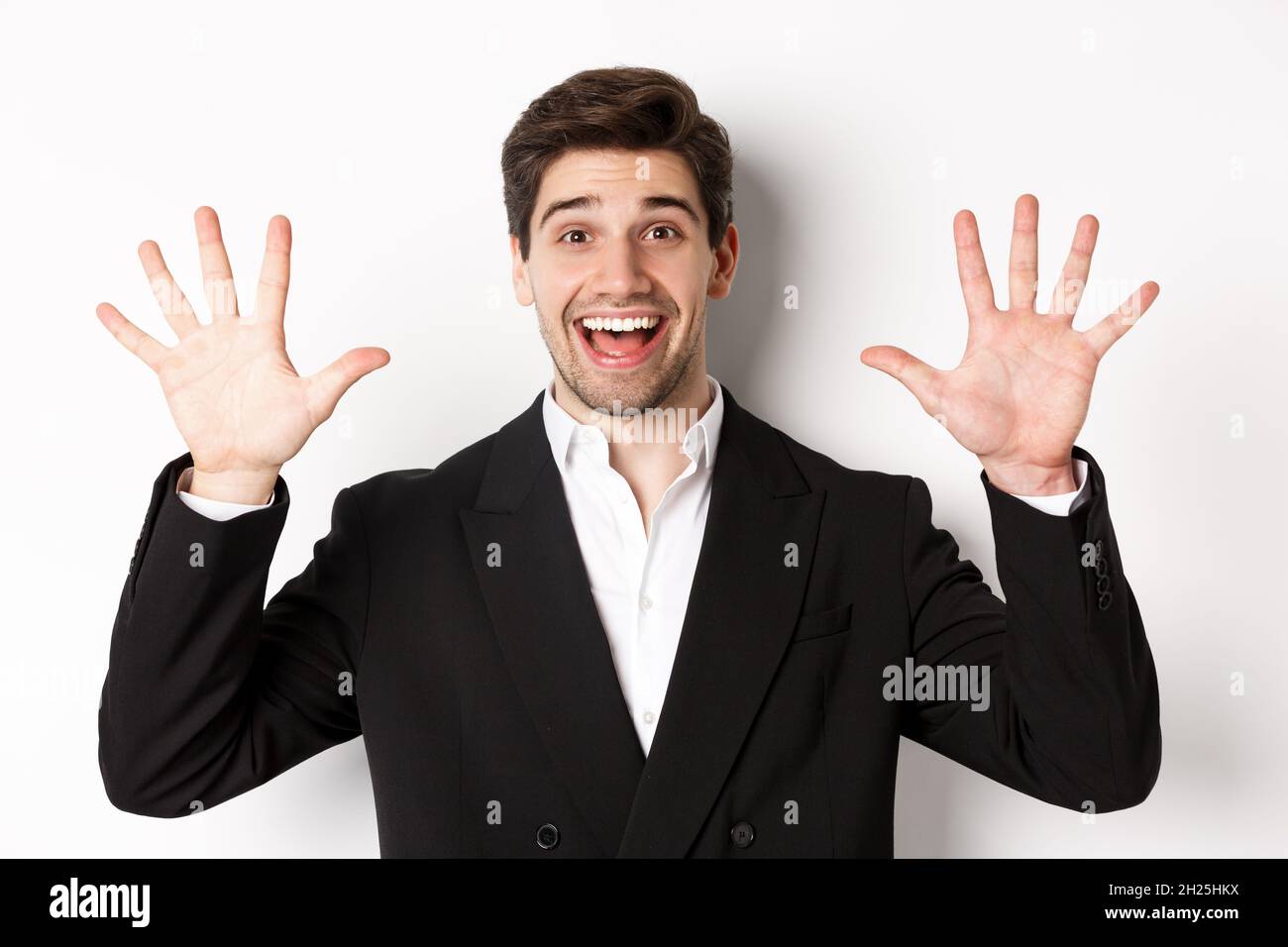 Close-up of handsome businessman in black suit, smiling amazed, showing ...