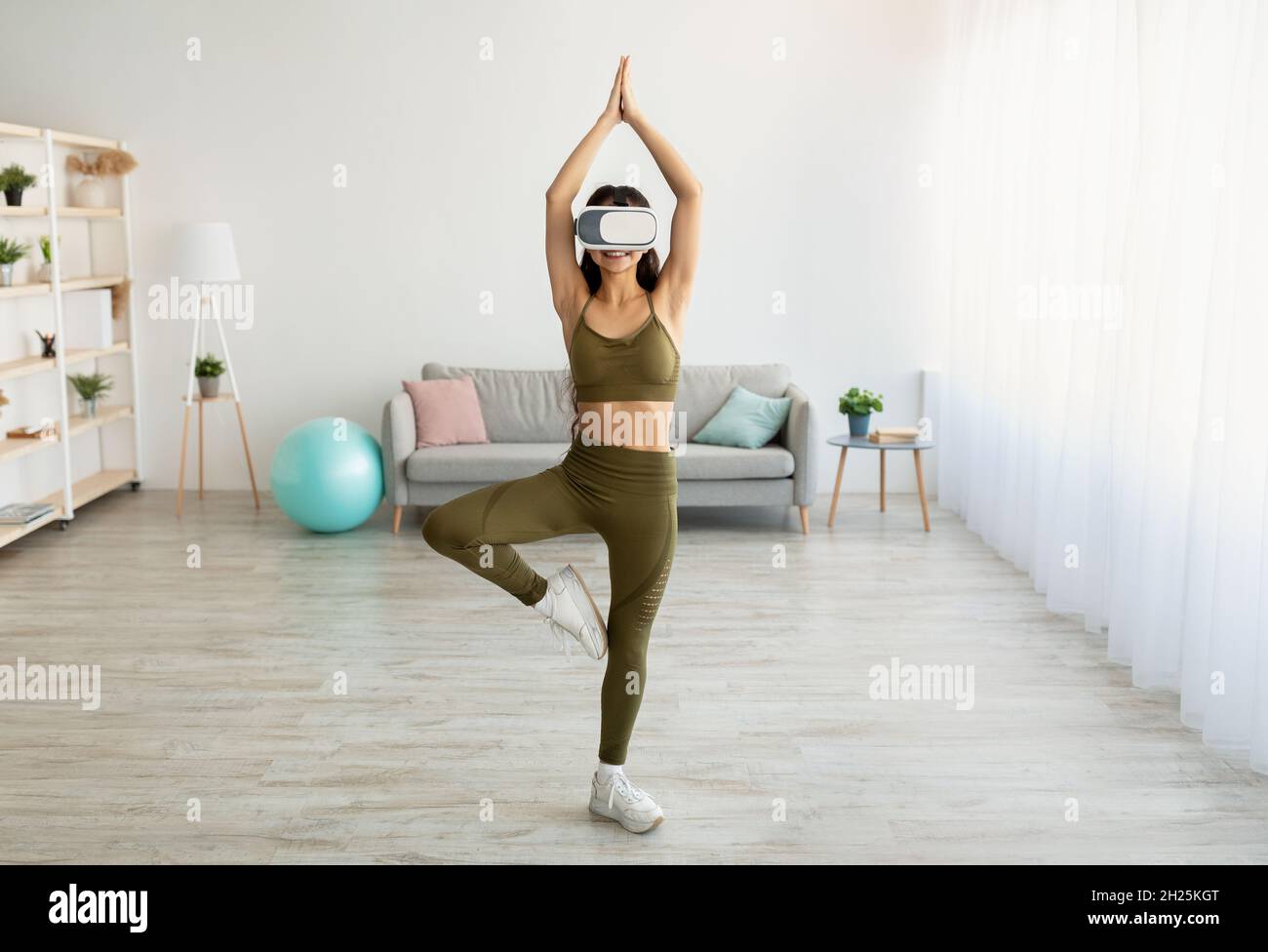 Full length of young fit Indian lady in VR headset doing virtual yoga ...