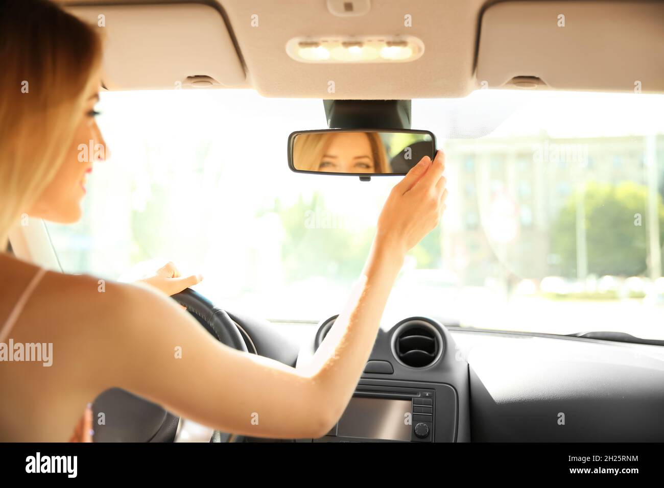 Young woman adjusting rearview mirror in car Stock Photo - Alamy