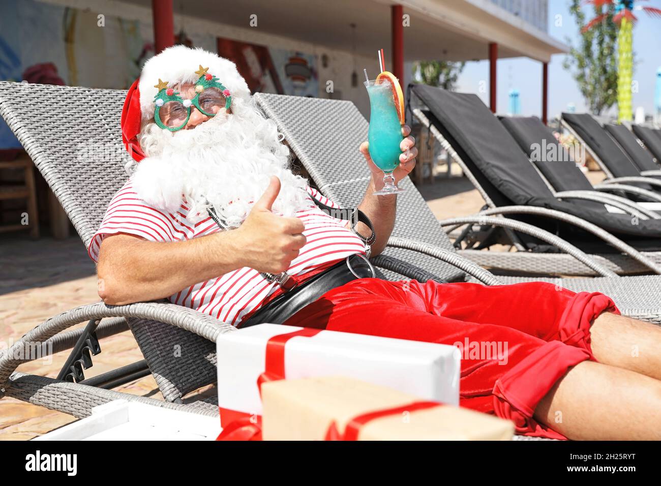 Authentic Santa Claus with cocktail resting on lounge chair at resort ...