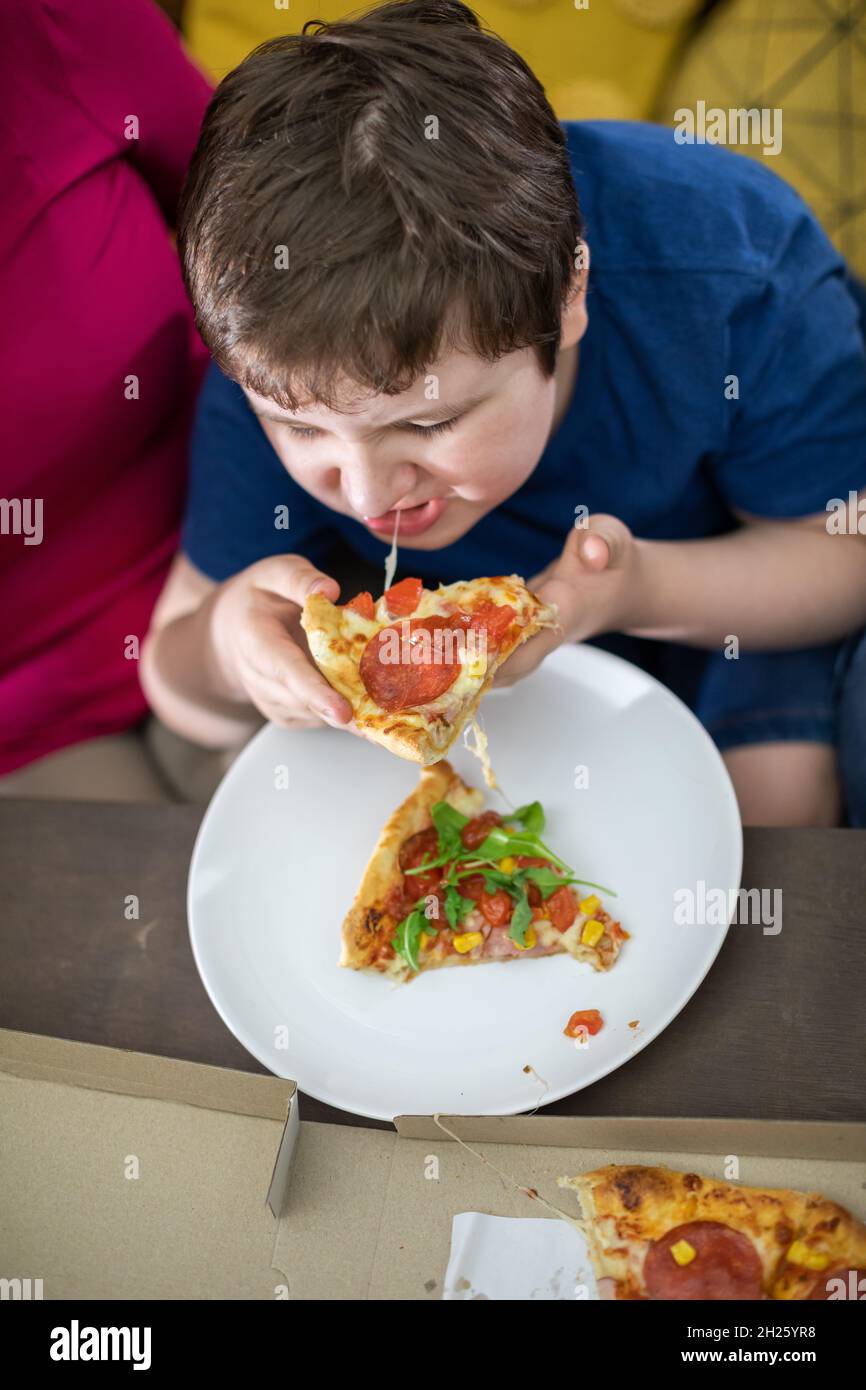 The child is eating pizza while sitting on the sofa and the dog is ...