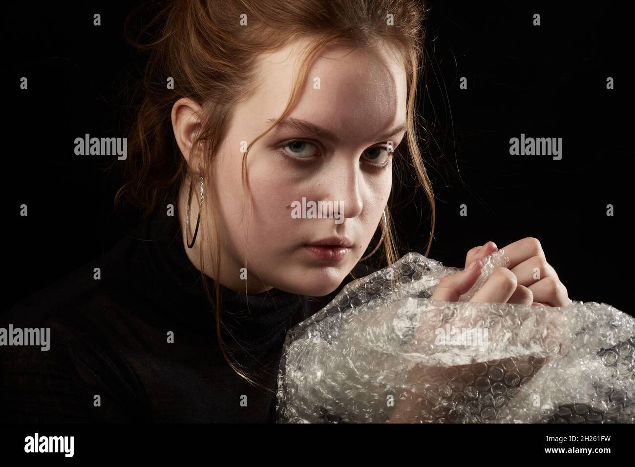 sad young woman with down syndrome popping plastic bubble wrap on black ...