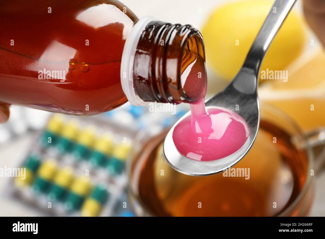 Pouring cough syrup from bottle into spoon on blurred background ...