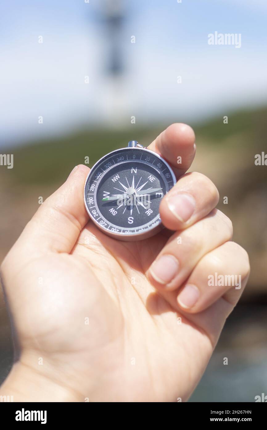 Closeup shot of a hand holding a compass in front of a lighthouse by ...