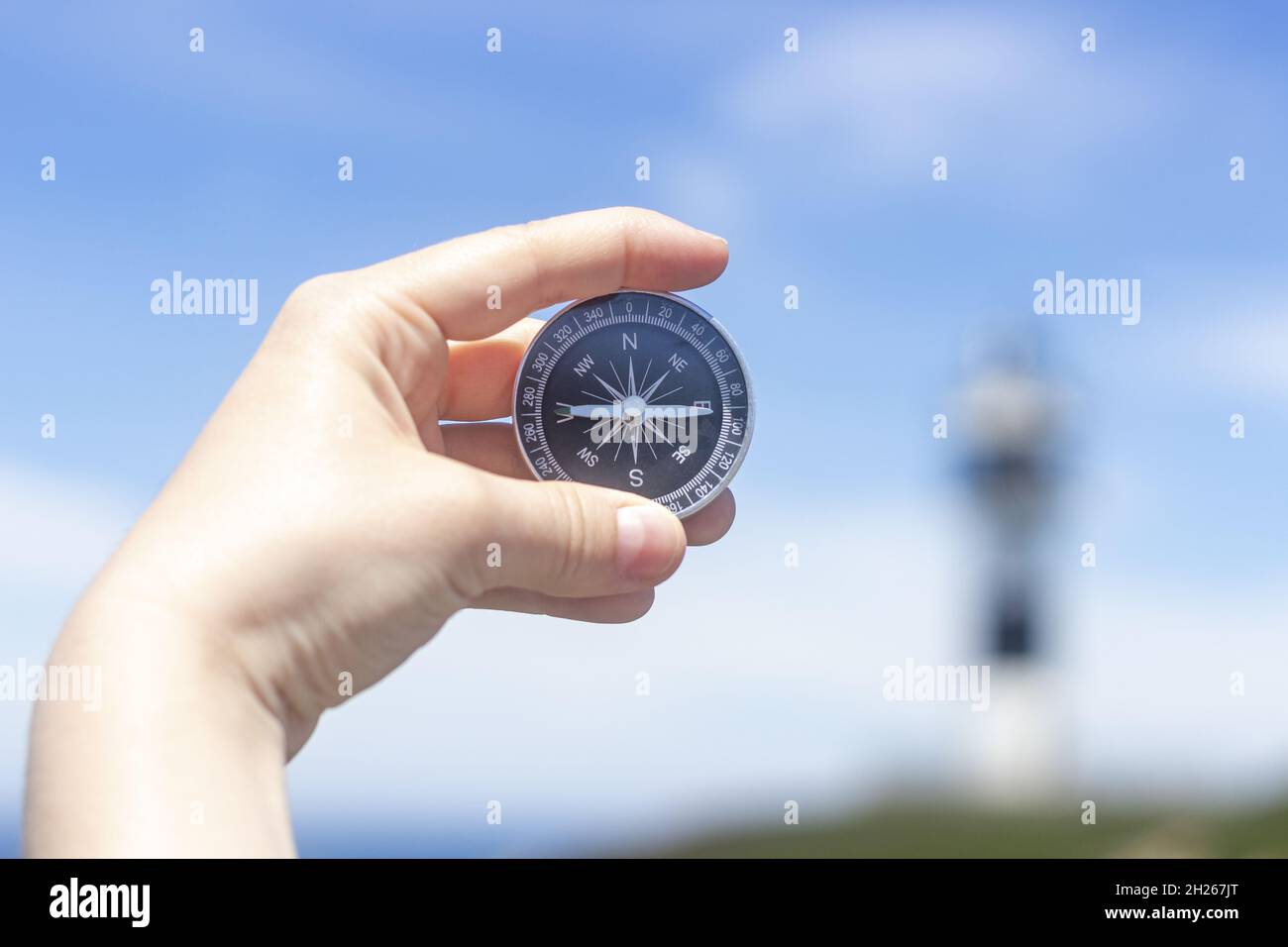 Closeup shot of a hand holding a compass in front of a lighthouse by ...