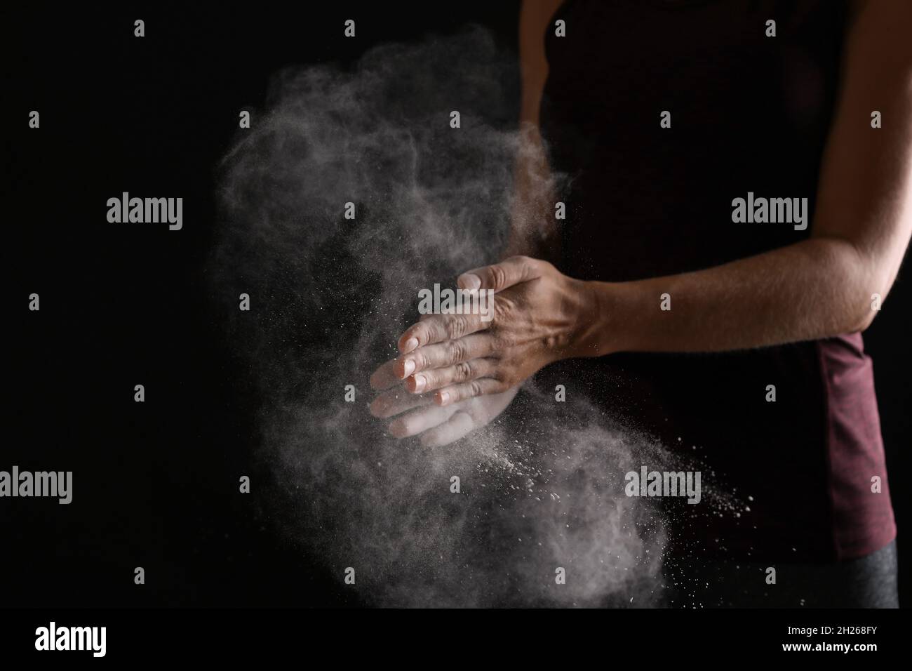 Young woman applying chalk powder on hands against dark background ...