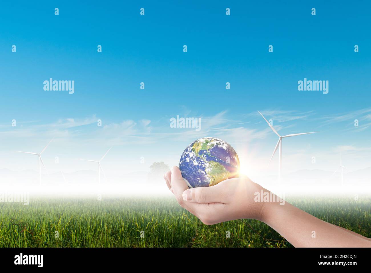 Hands holding earth, globe on wind turbine field against blue sky ...