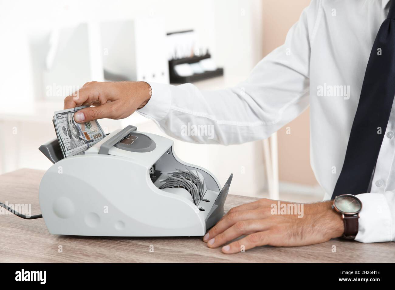 Male teller putting money into currency counting machine at cash ...