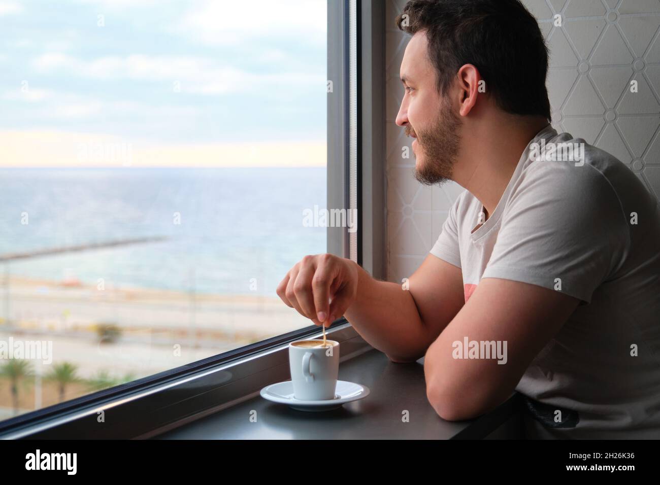 Young caucasian man drink coffee look at the sunrise and sea throw the ...