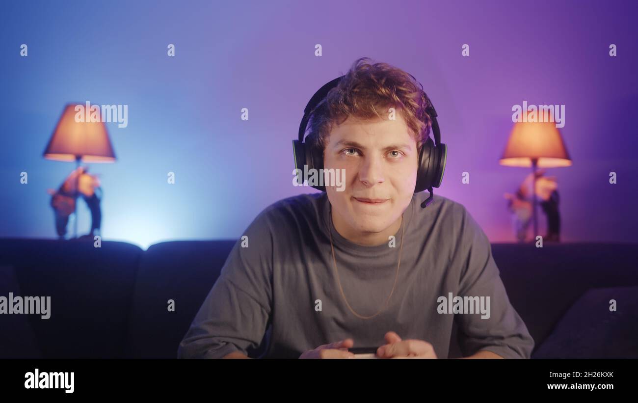 Handsome blonde-hair young gamer boy sitting on couch and playing game ...