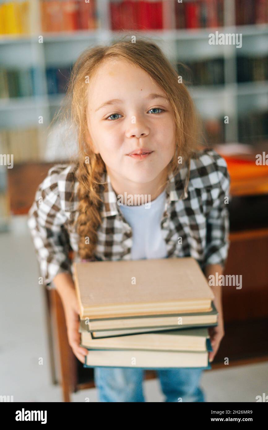 Vertical portrait of playful elementary child school girl holding stack ...