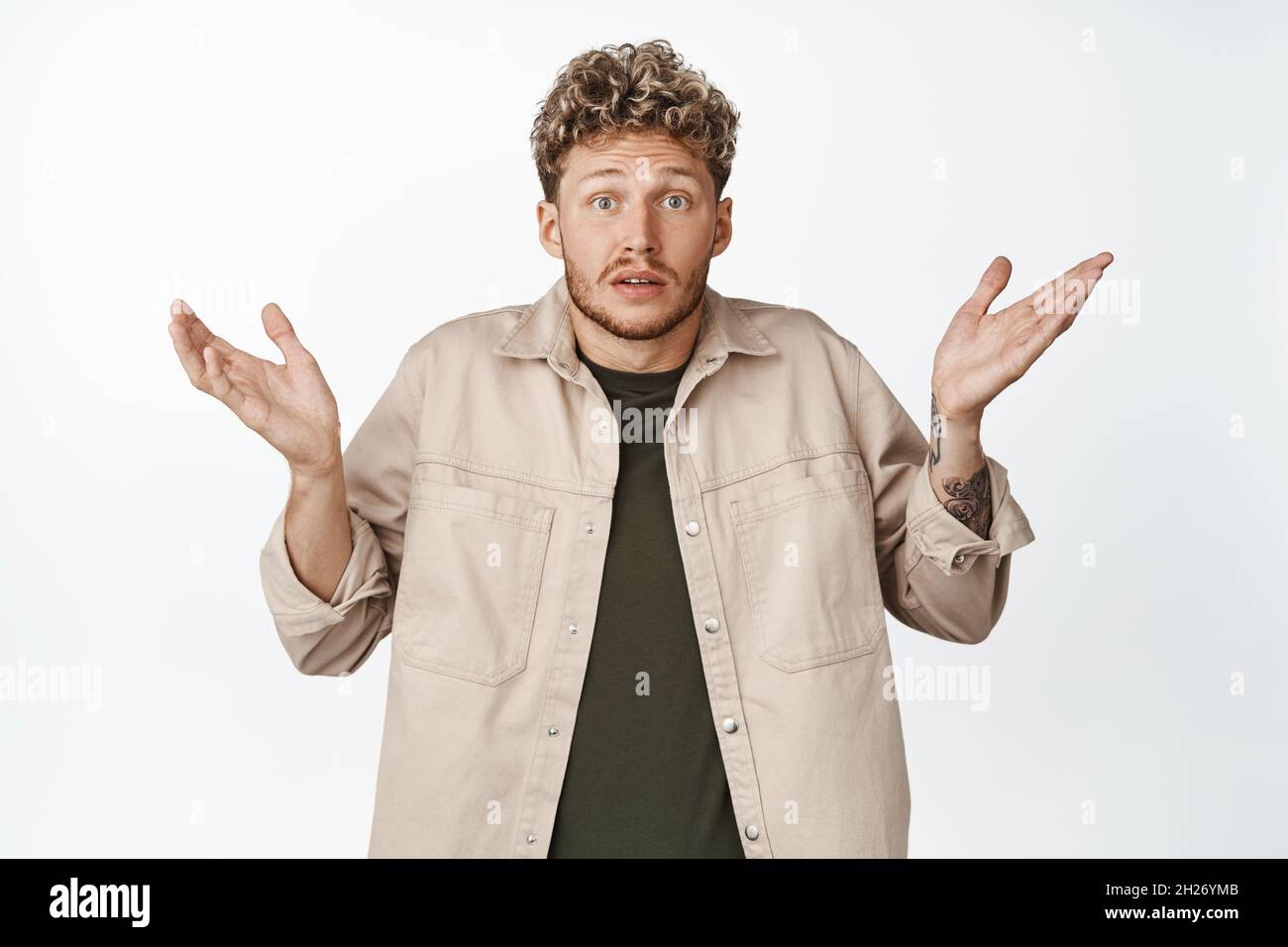 Confused young blond man shrugging shoulders and raise hands up, dont ...