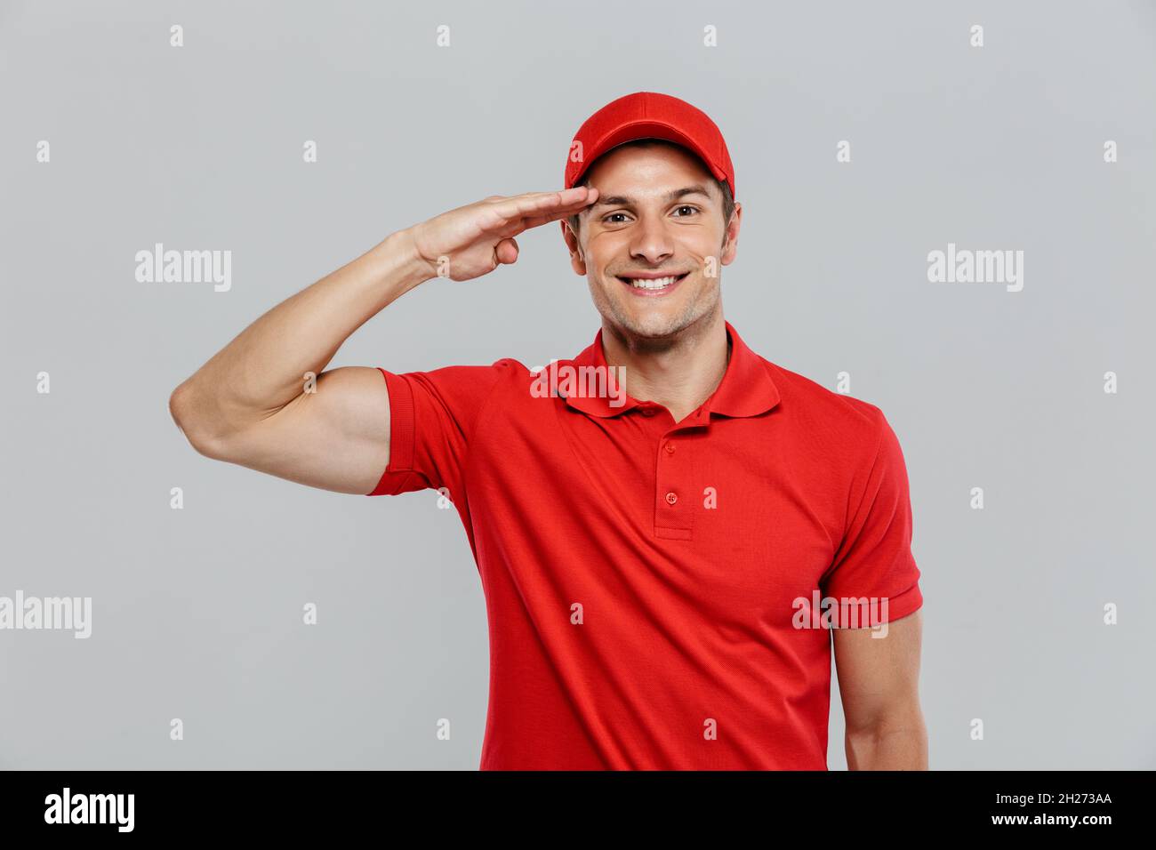Young delivery man wearing uniform saluting and smiling at camera ...