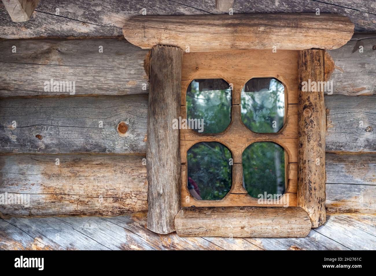 Small window on the wall of a log house, the reflection of green trees ...