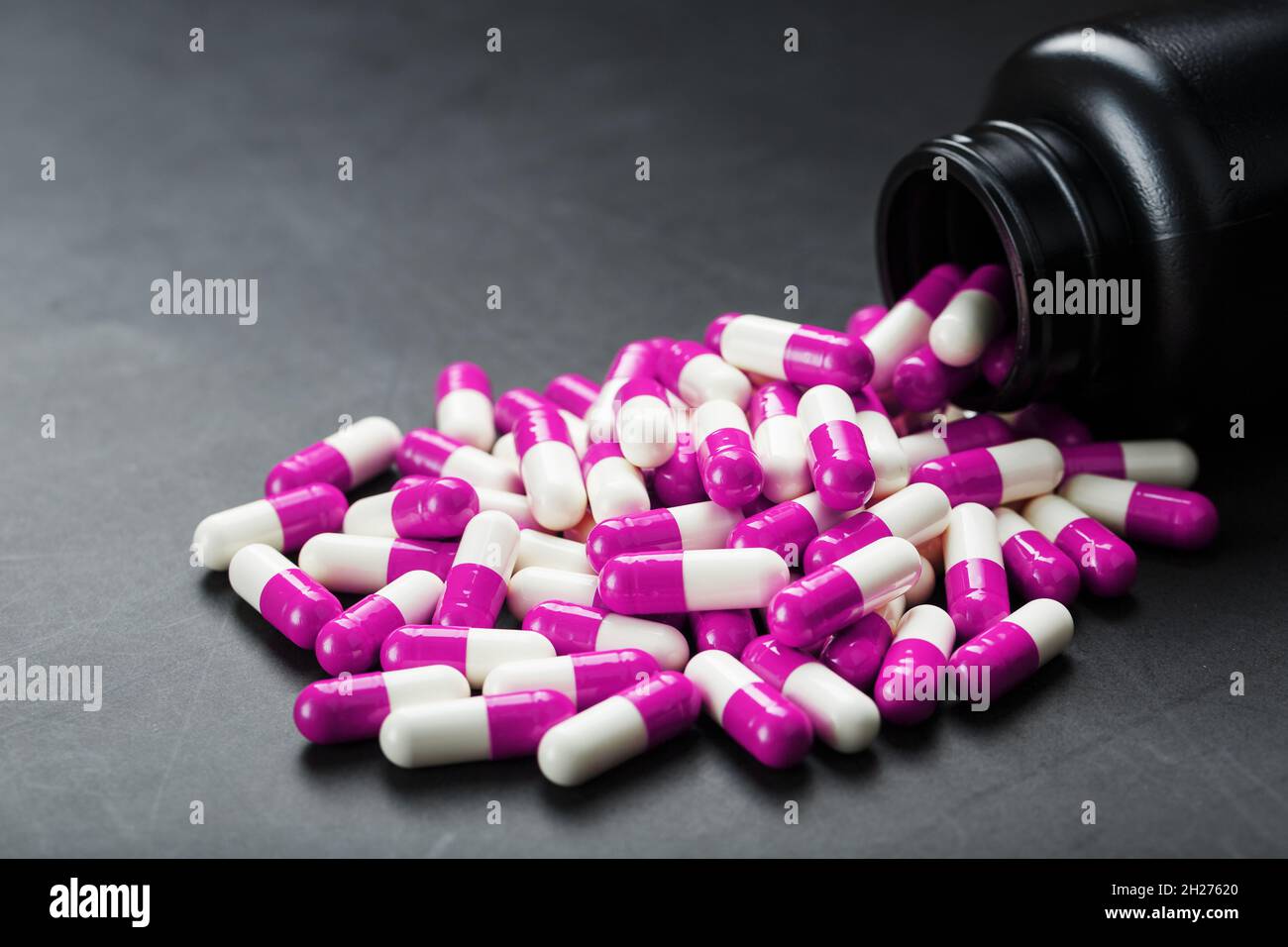 Pink pills with medicines are scattered from a black jar on a black ...