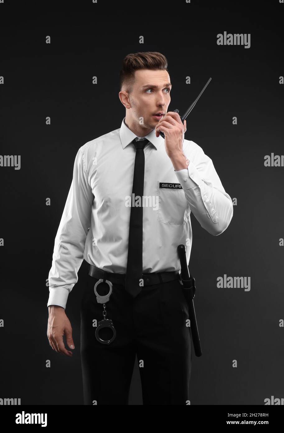 Male security guard using portable radio transmitter on dark background ...