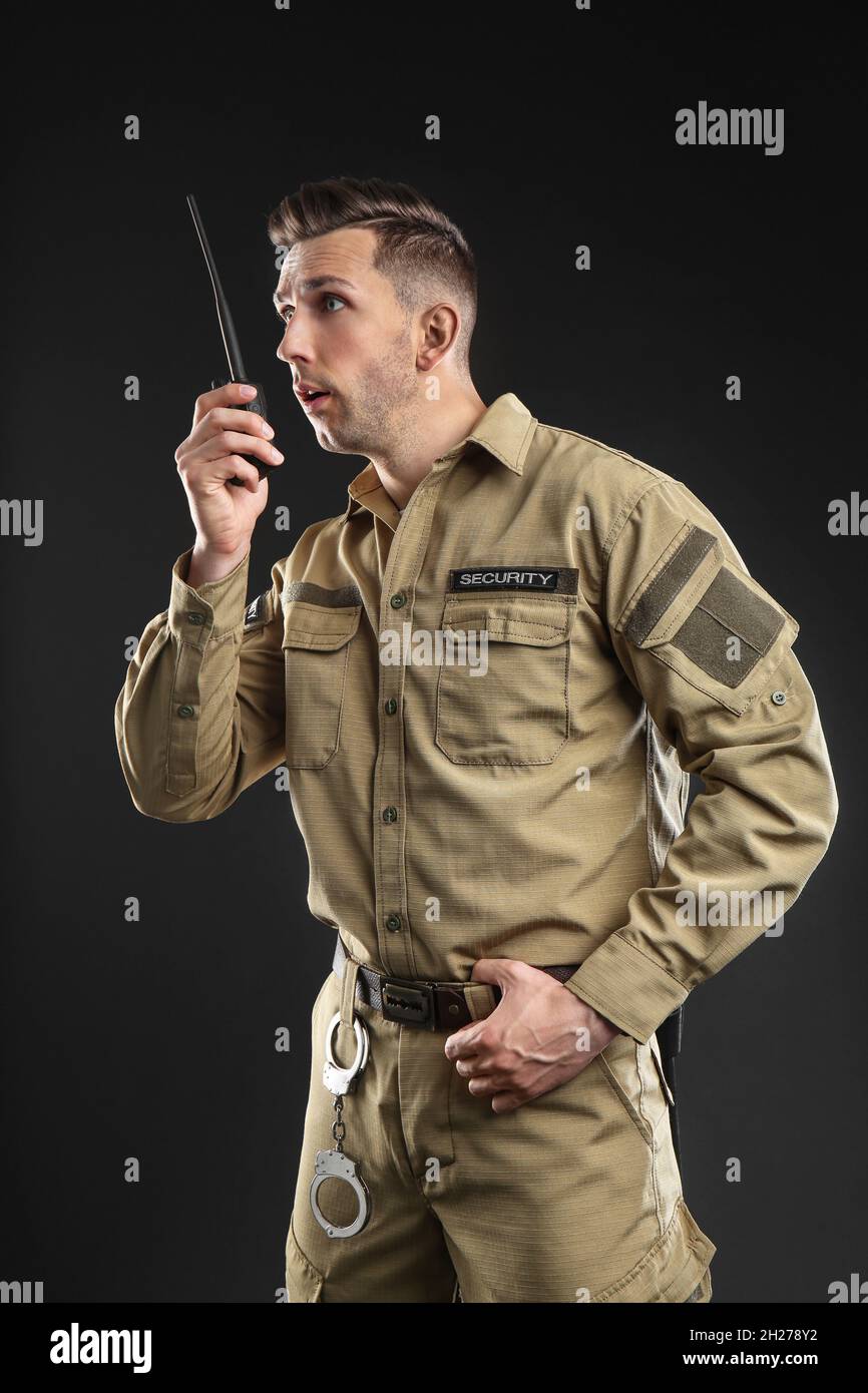 Male security guard using portable radio transmitter on dark background ...