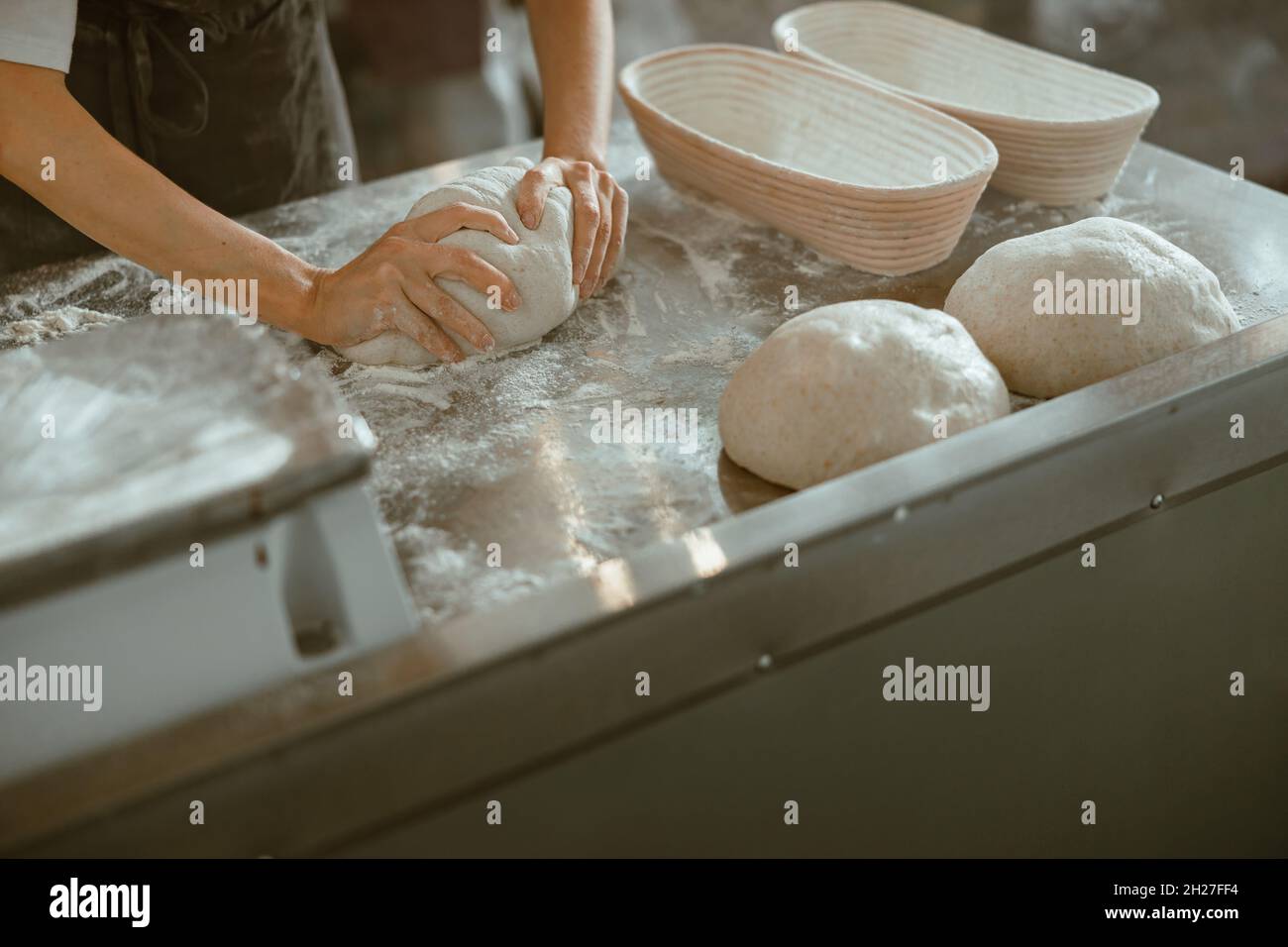 Worker kneads dough making bread at metal table in modern craft bakery ...