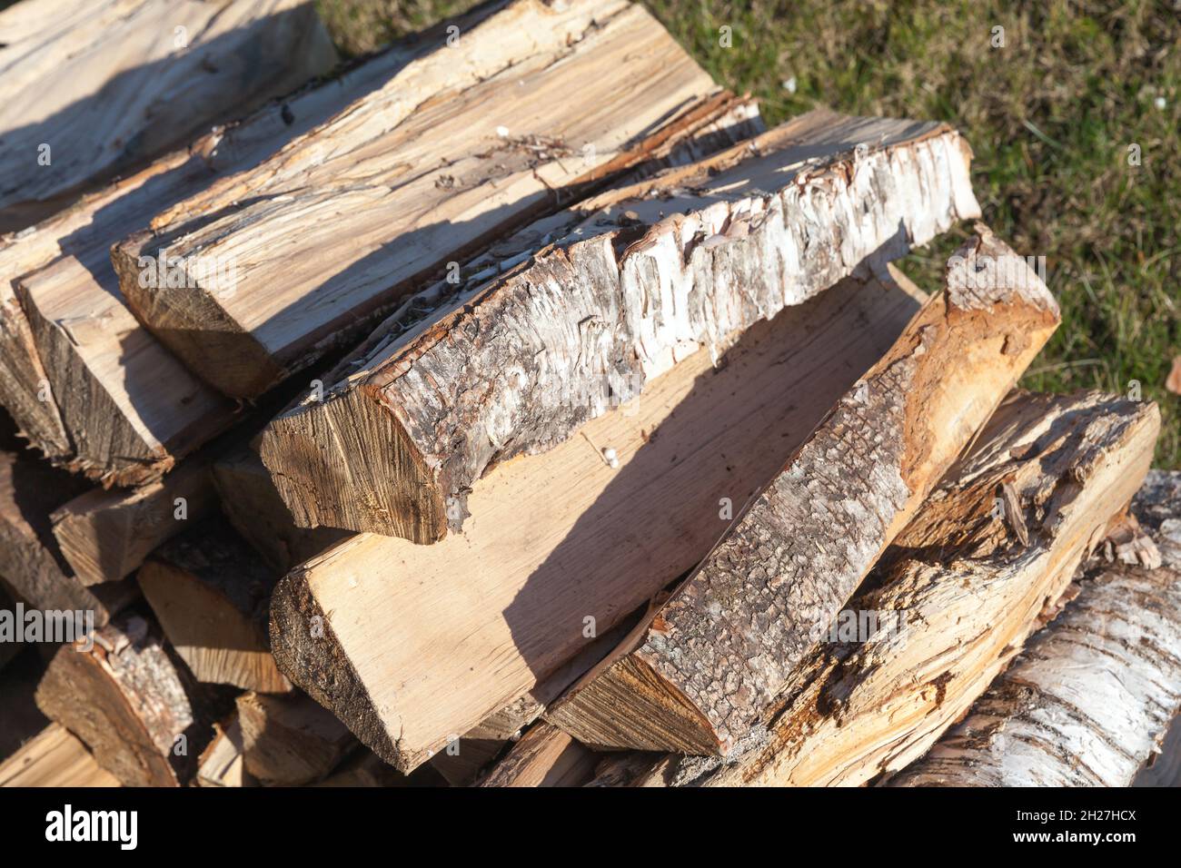 Pile of firewood, birch chocks lay stacked in a sunlight, outdoor photo ...