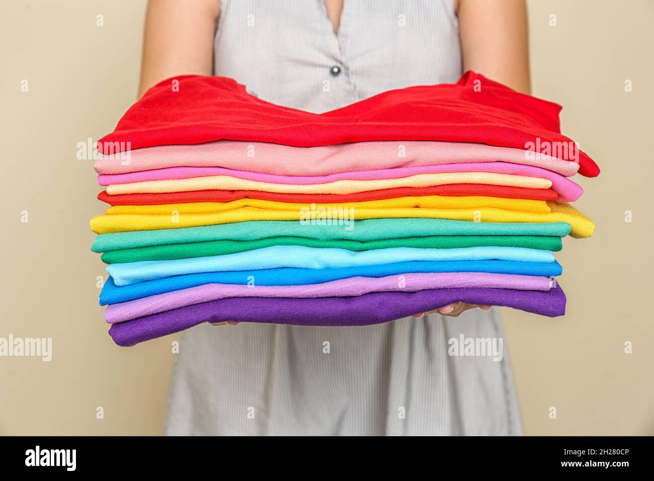 Woman holding stack of colorful t-shirts on light background Stock ...