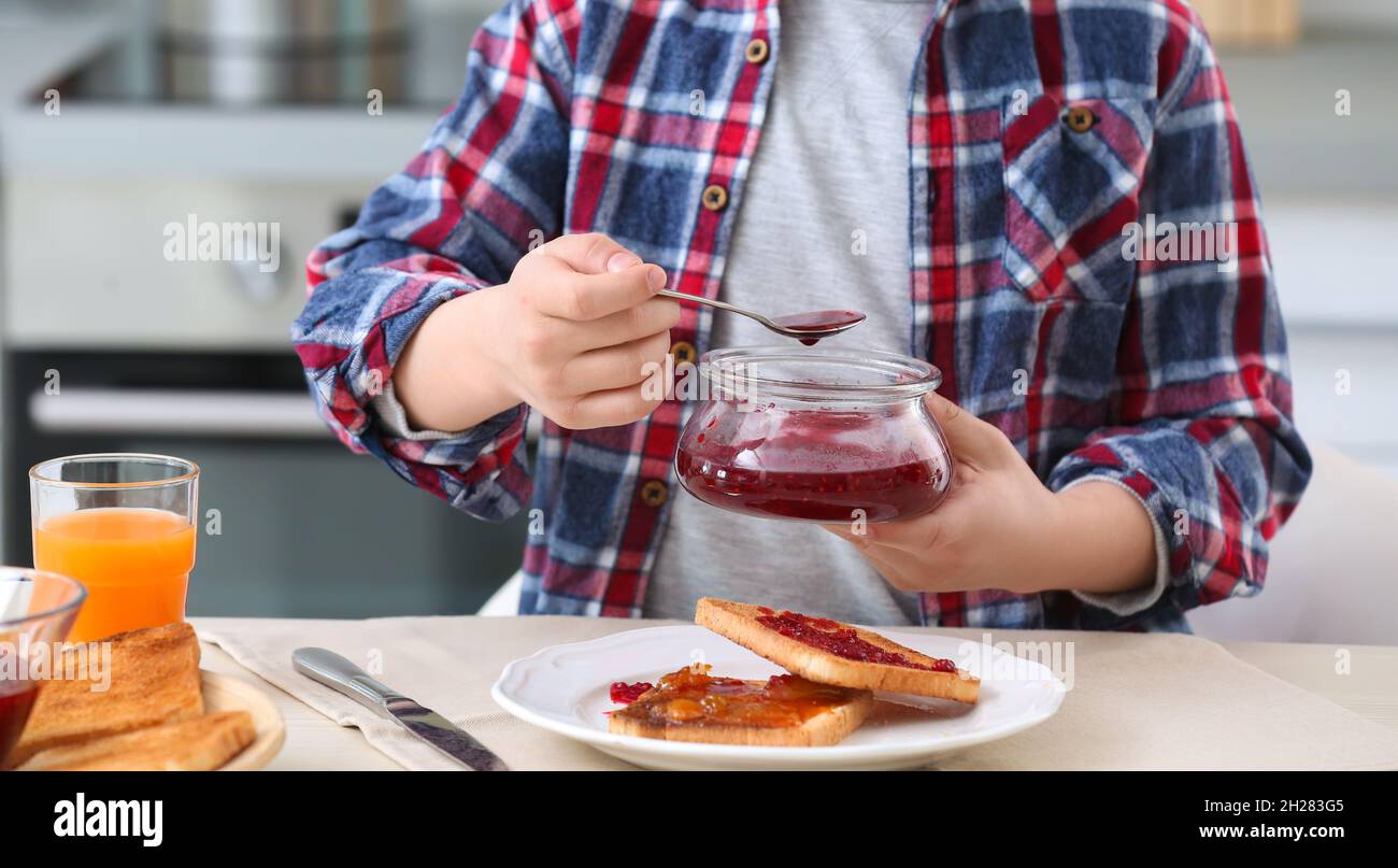 Cute little boy spreading jam onto tasty toasted bread at table in ...