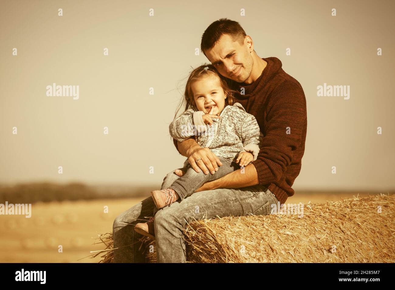 Happy father and two year old girl sitting on hay bale in harvested ...