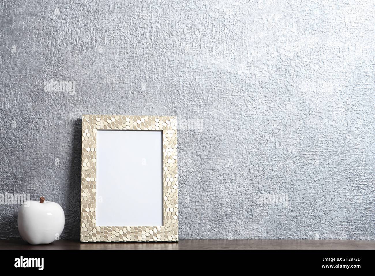 Blank frame and decorative apple figure on table near color wall. Mock ...
