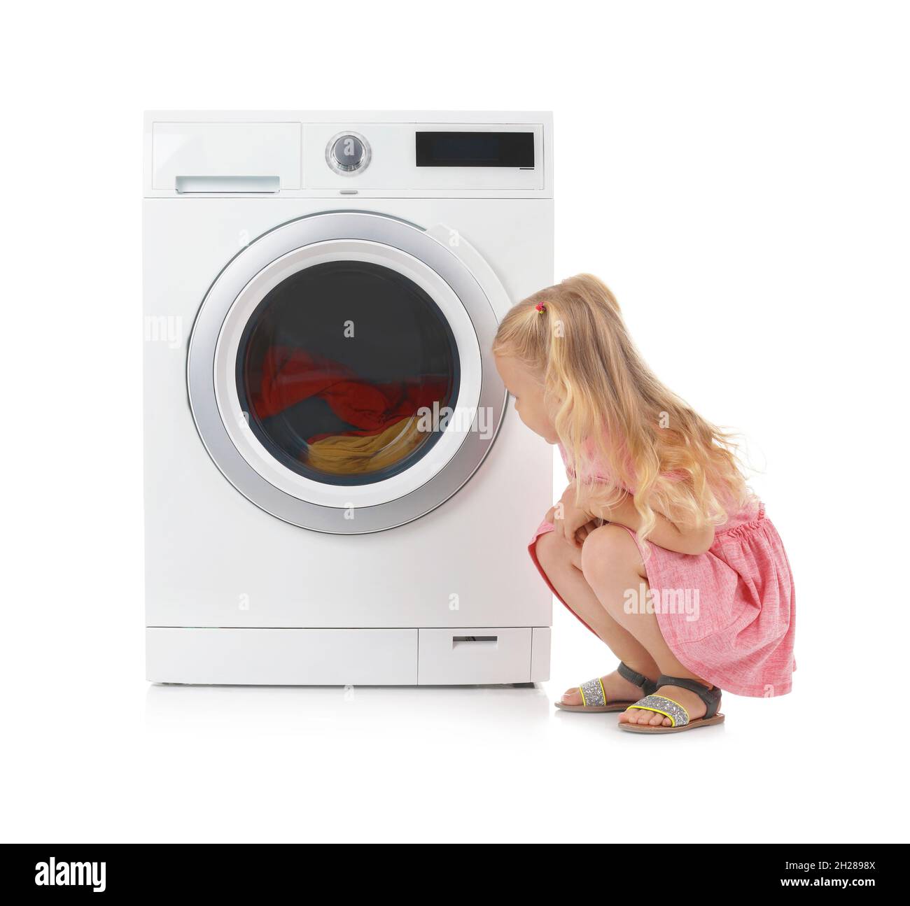 Cute little girl near washing machine with laundry on white background ...
