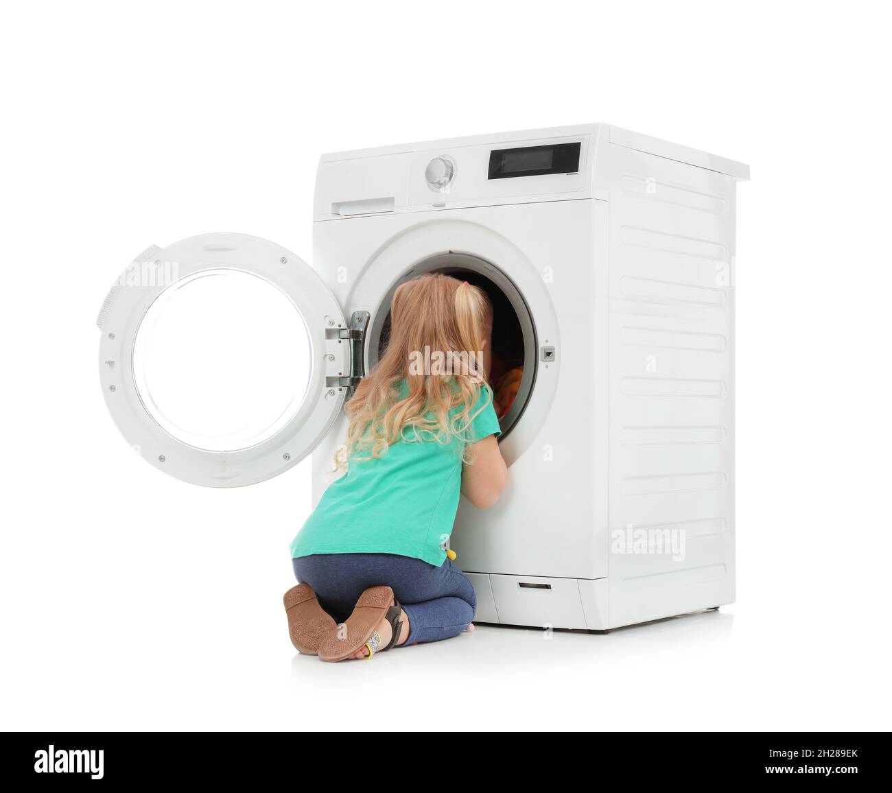 Cute little girl looking into washing machine with laundry on white ...