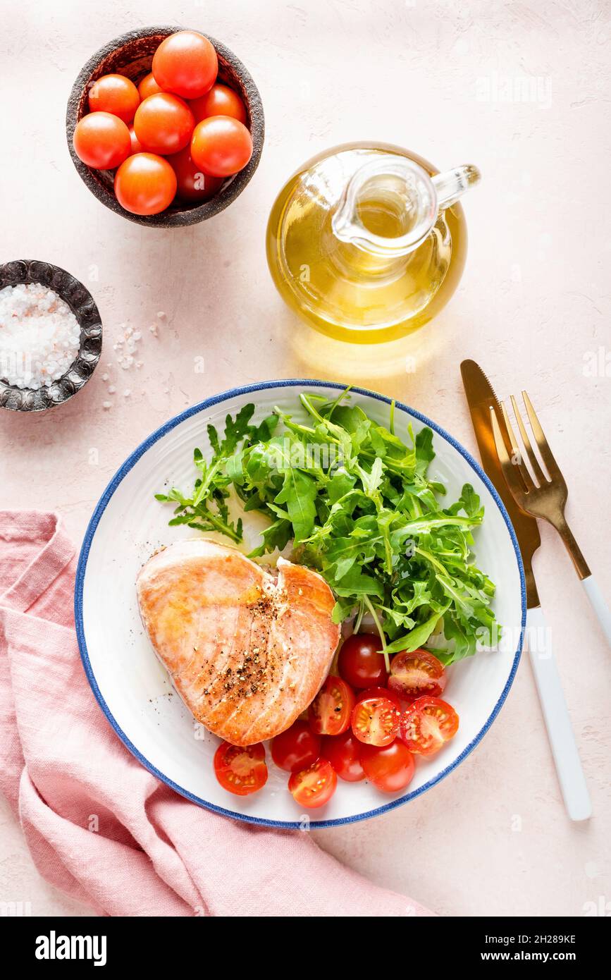 Pink tuna steak served with arugula and tomatoes. Healthy balanced meal ...