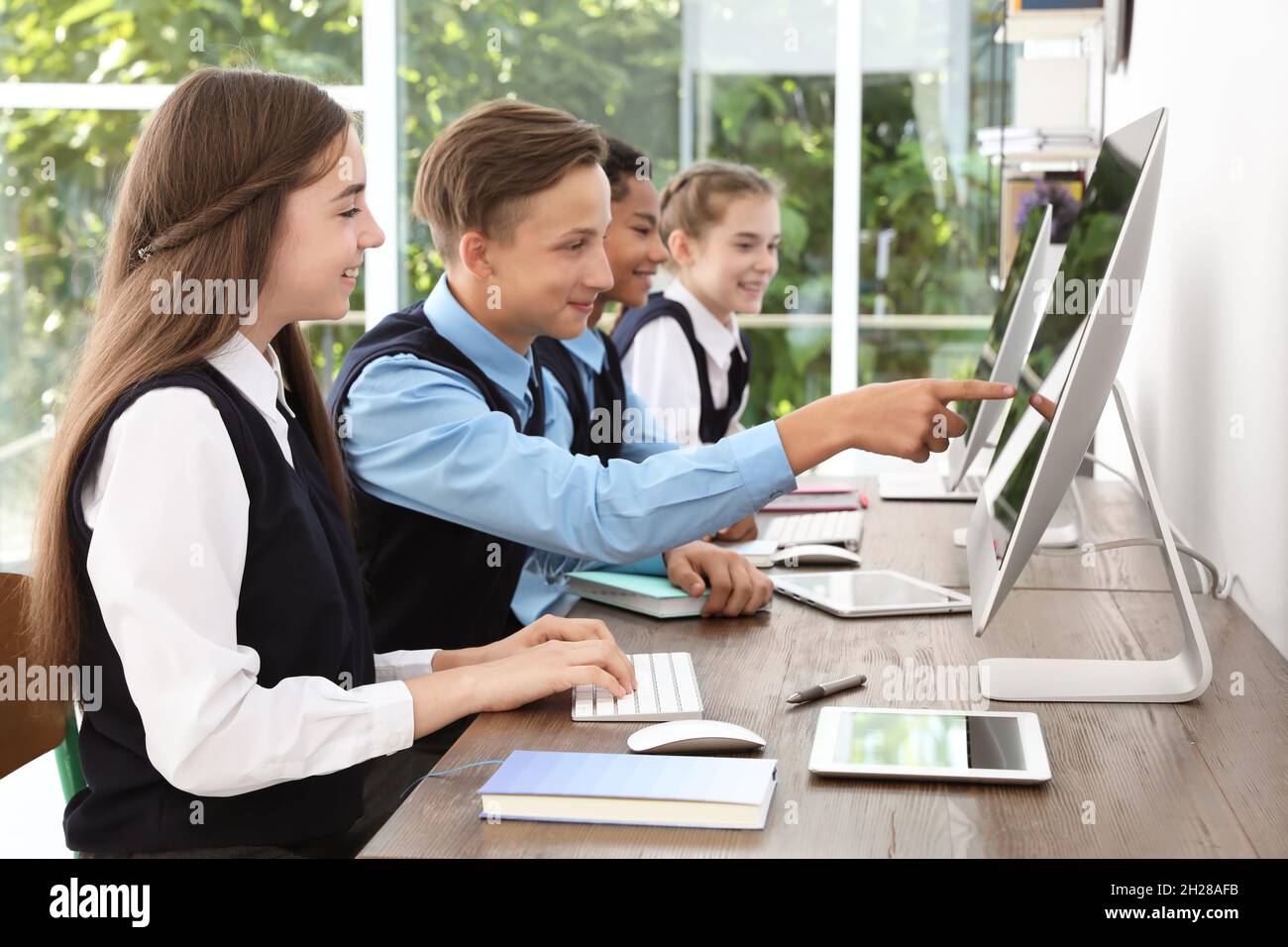Teenage students in stylish school uniform at desks with computers ...