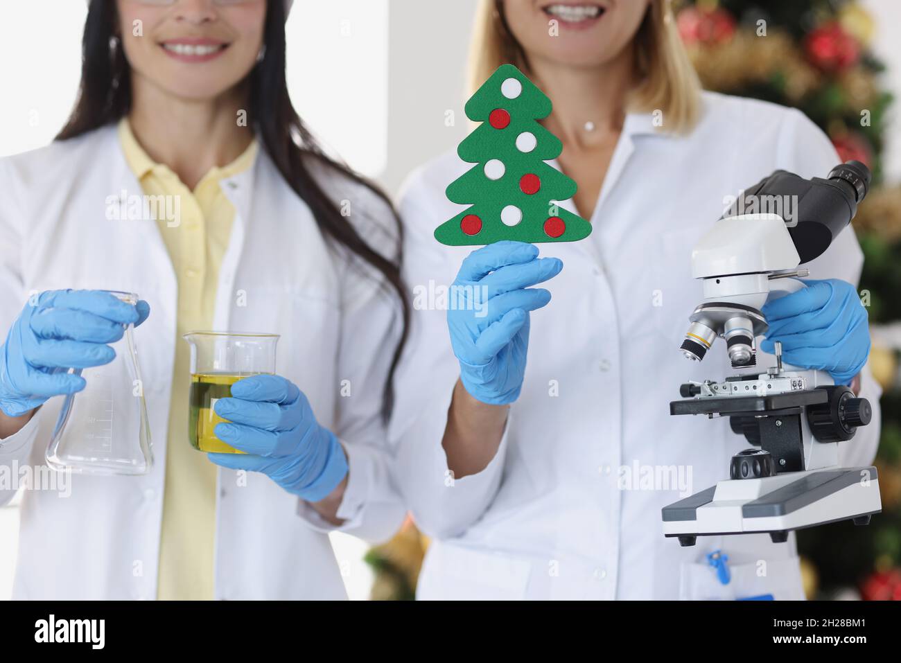 Two women in laboratory are holding microscope and test tubes closeup ...