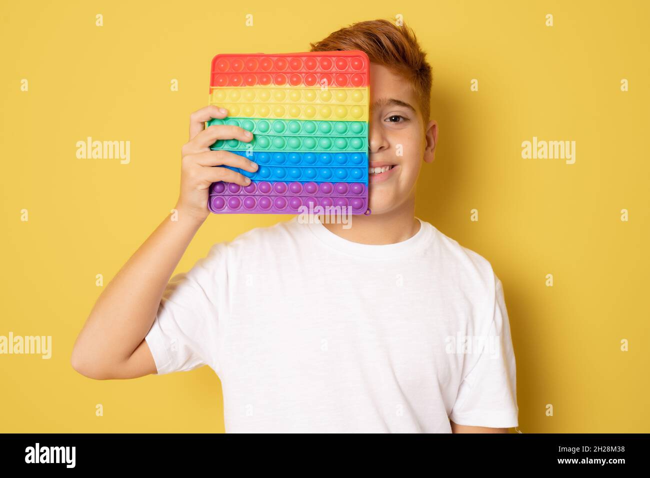happy boy holding pop it game in hands, isolated on yellow background ...