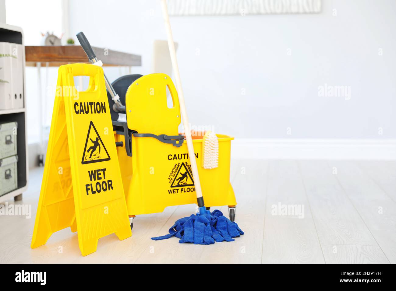Phrase "CAUTION WET FLOOR" on safety sign and mop bucket with cleaning ...