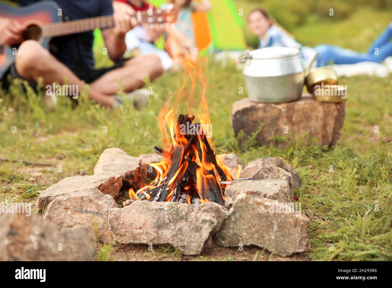 Group of people resting outdoors, focus on bonfire. Camping season ...