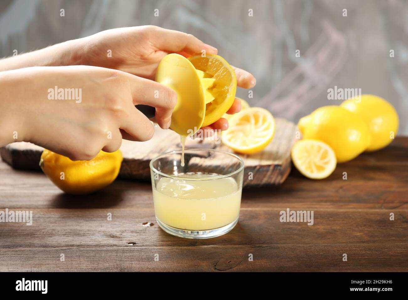 Young woman squeezing lemon juice with reamer into glass on table Stock Photo - Alamy