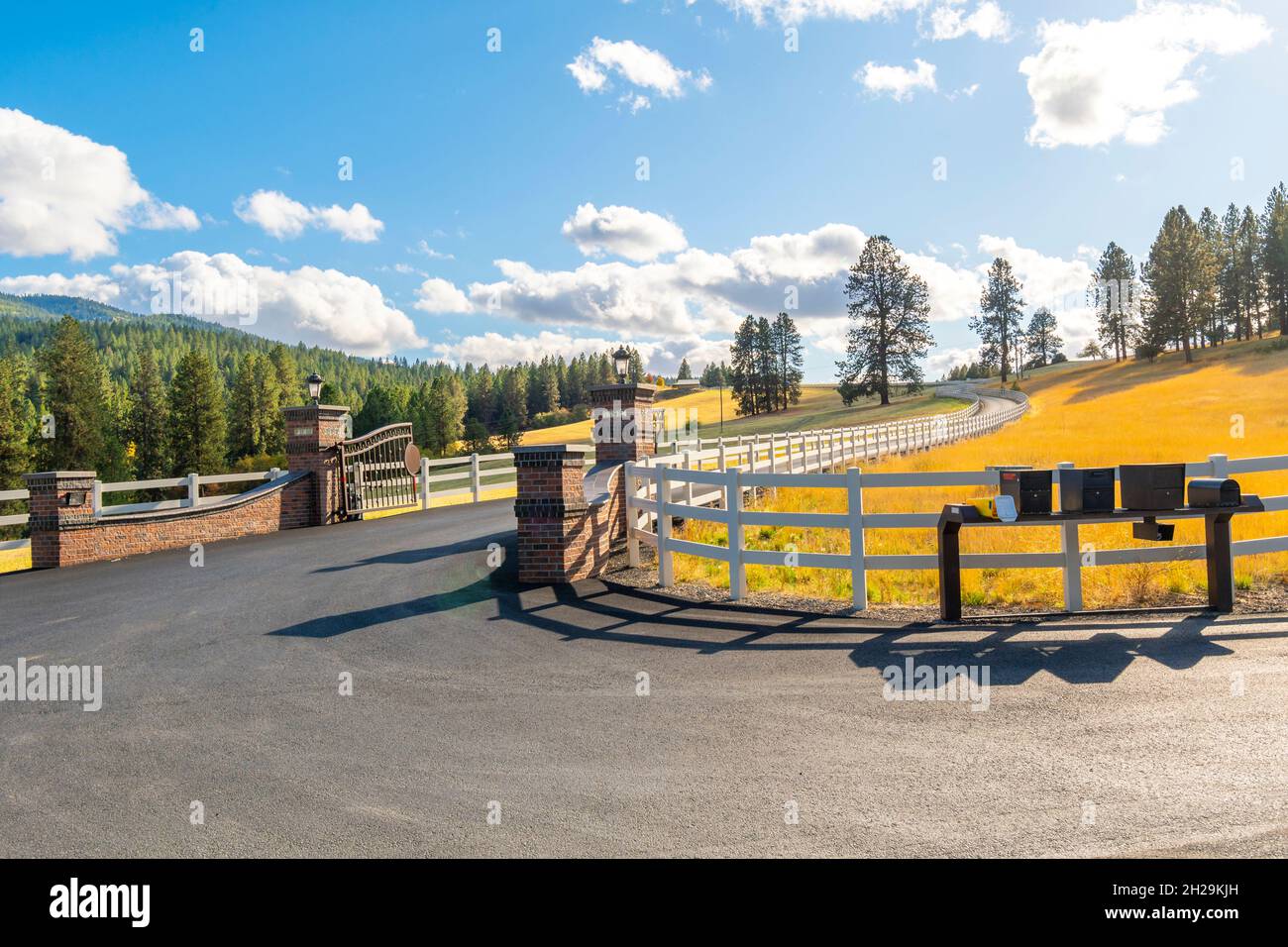 A winding gated road or path with white fence in a rural community of ...