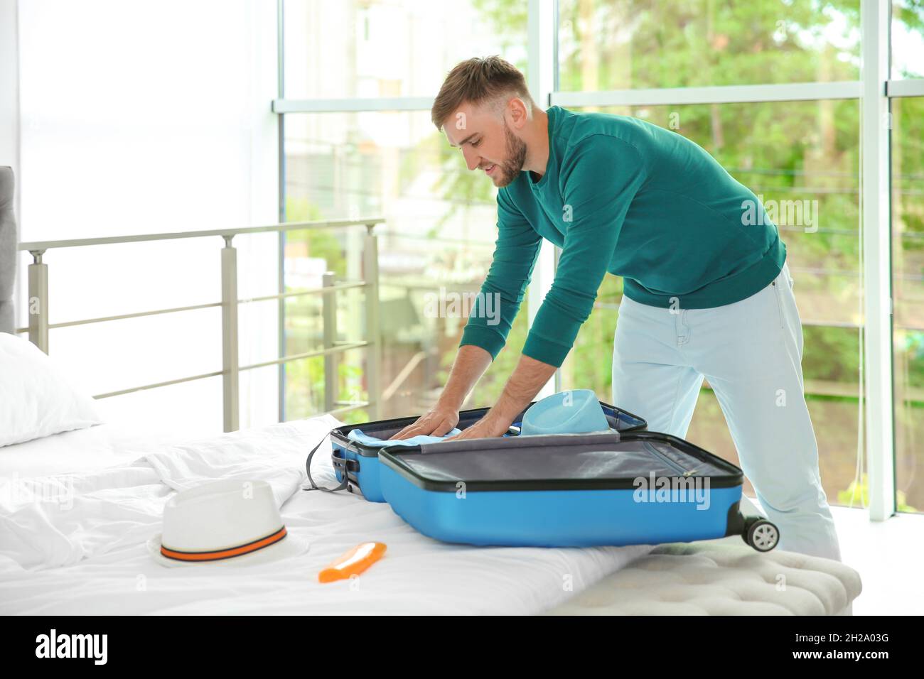 Young man packing suitcase for summer journey on bed Stock Photo - Alamy