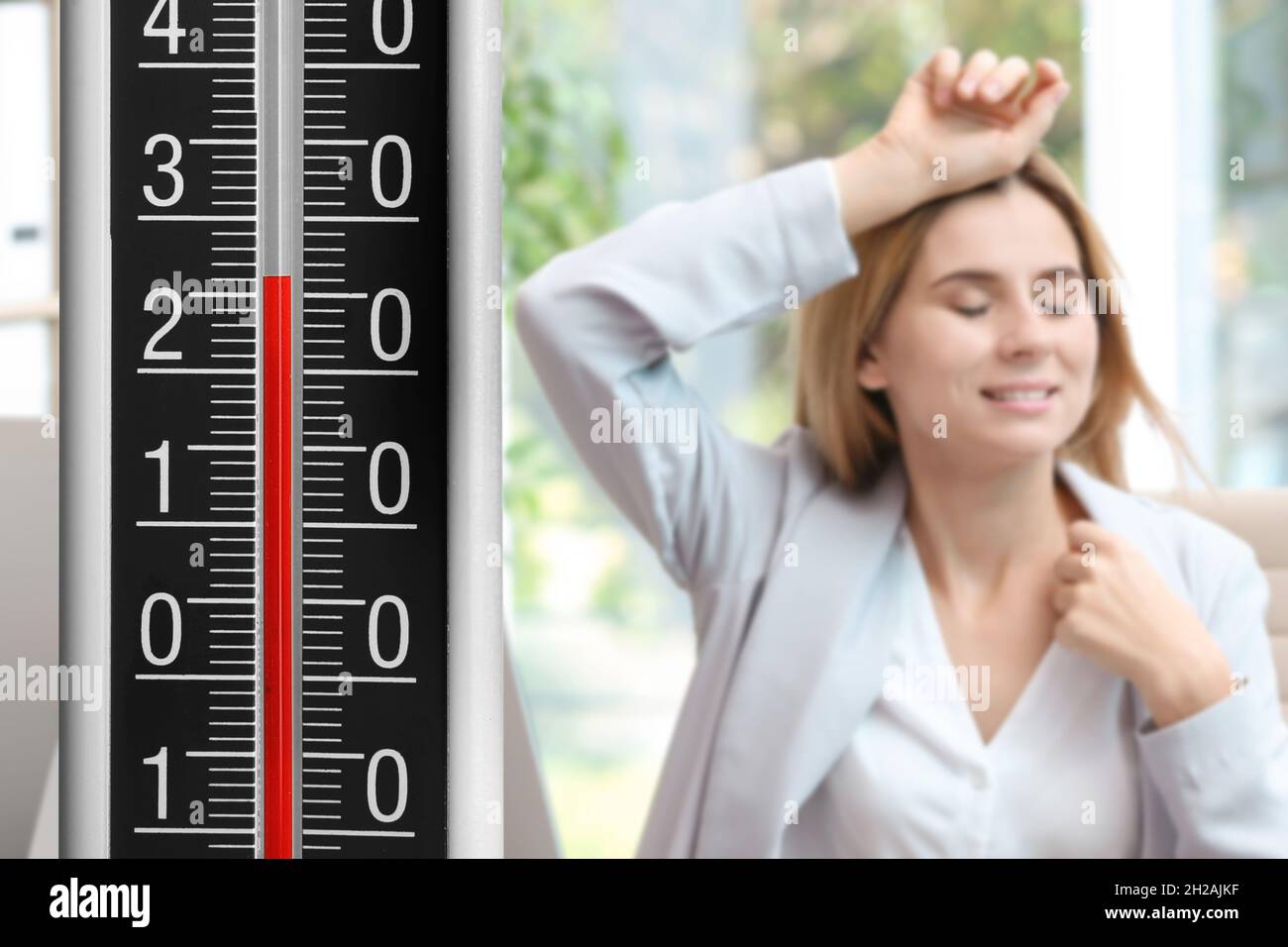 High temperature on thermometer and woman suffering from heat in office ...